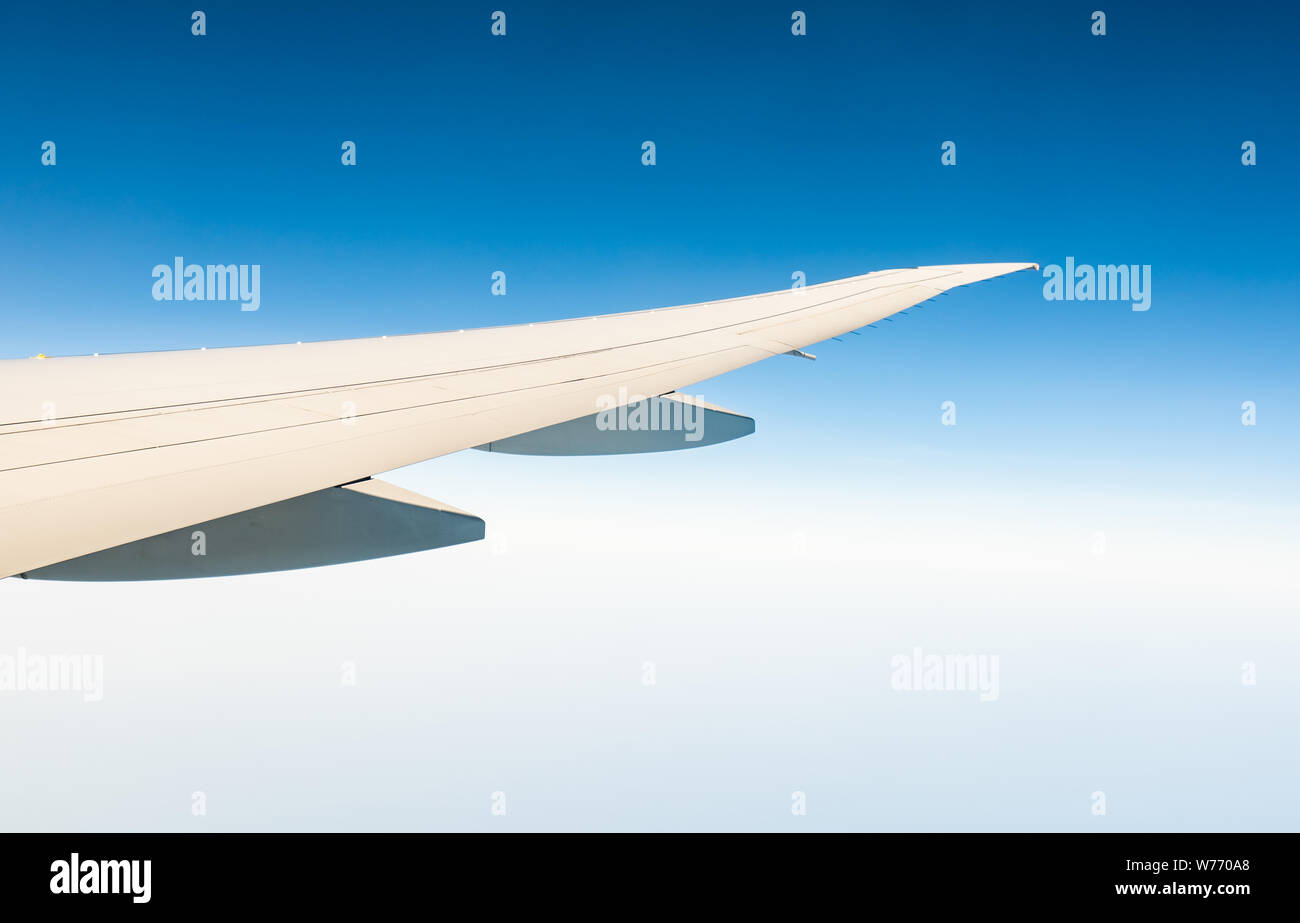 Wing of plane over white clouds. Airplane flying on clear blue sky ...