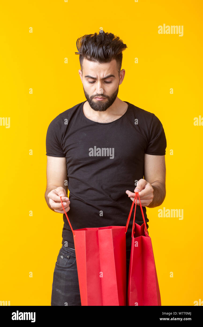 Cute young sad bearded man looks at the purchase in shopping bags on a ...