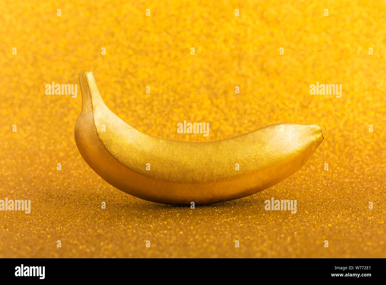 Gold colour food, golden banana on bright glitter or shimmer background ...