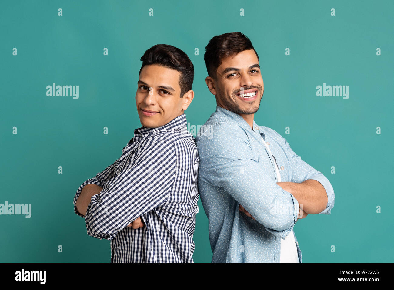 Two Latin Guys Standing Back-To-Back On Turquoise Studio Background ...