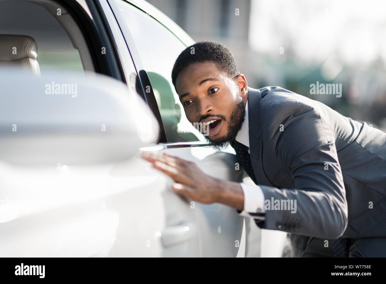 Visiting car dealership. Afro man hugging his new car Stock Photo - Alamy