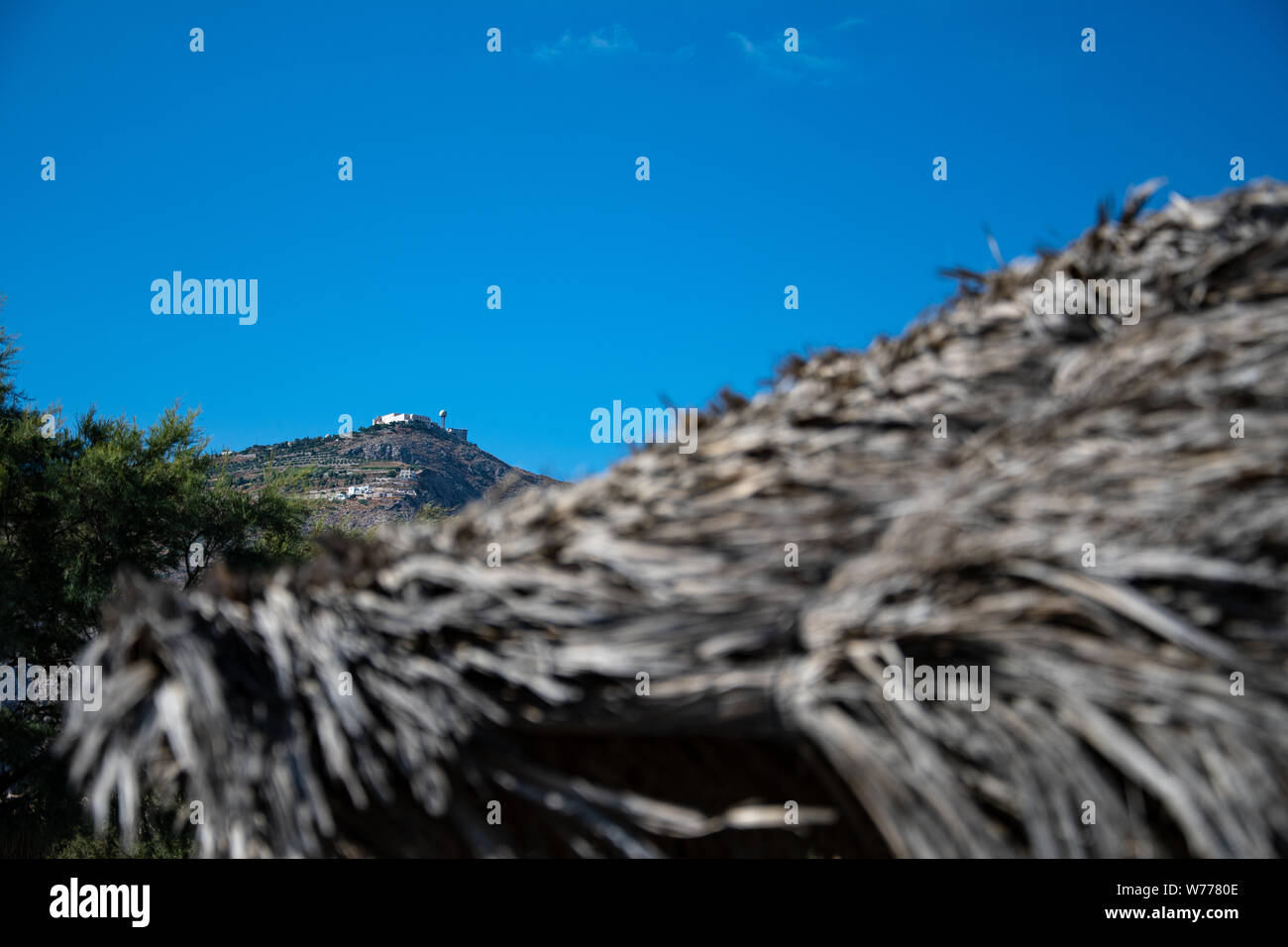 A straw parasol, a tree and The monastery of Prophet Elias atop ...