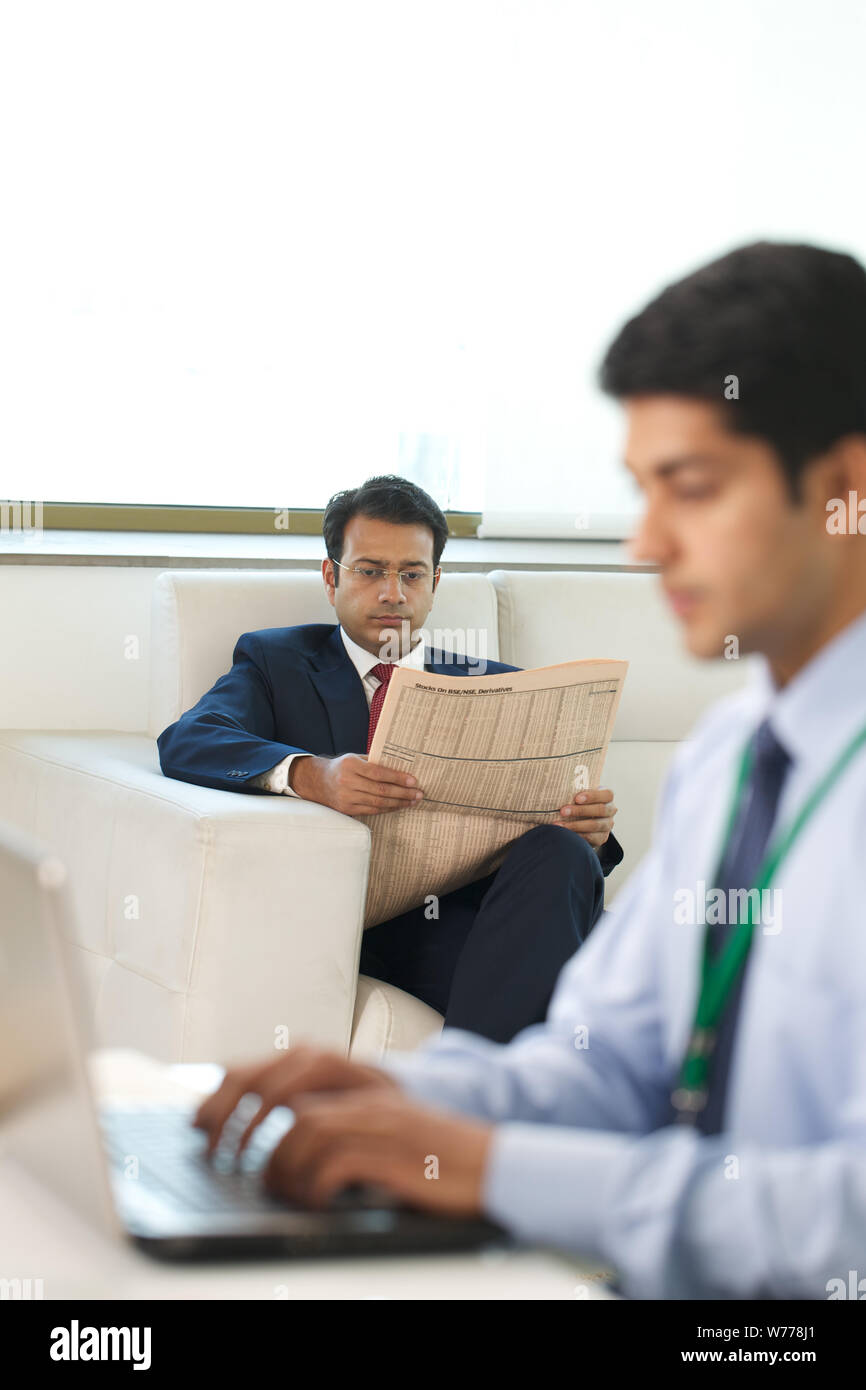Indian financial advisor working on a laptop with a businessman reading ...