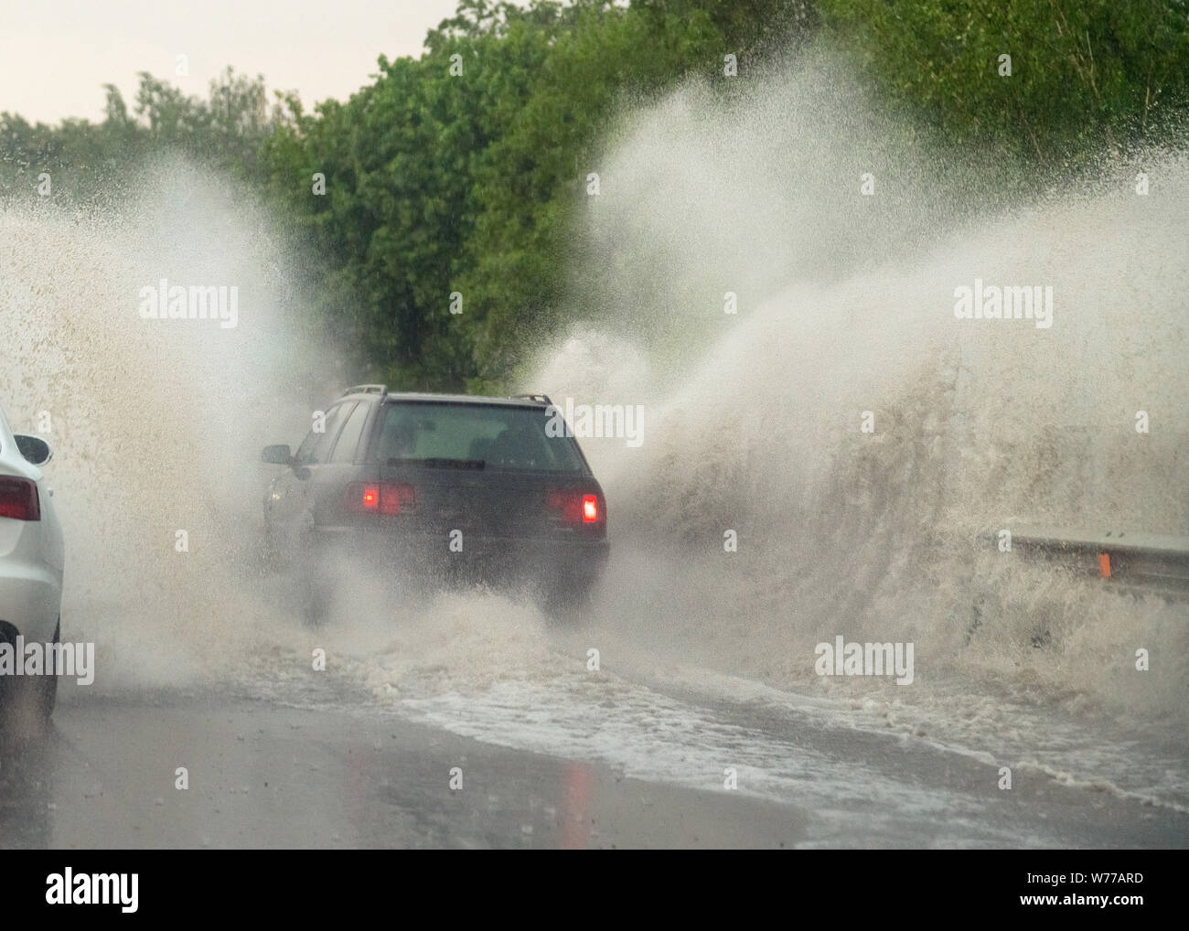 Car runs into big puddle at heavy rain, water splashing over the car ...