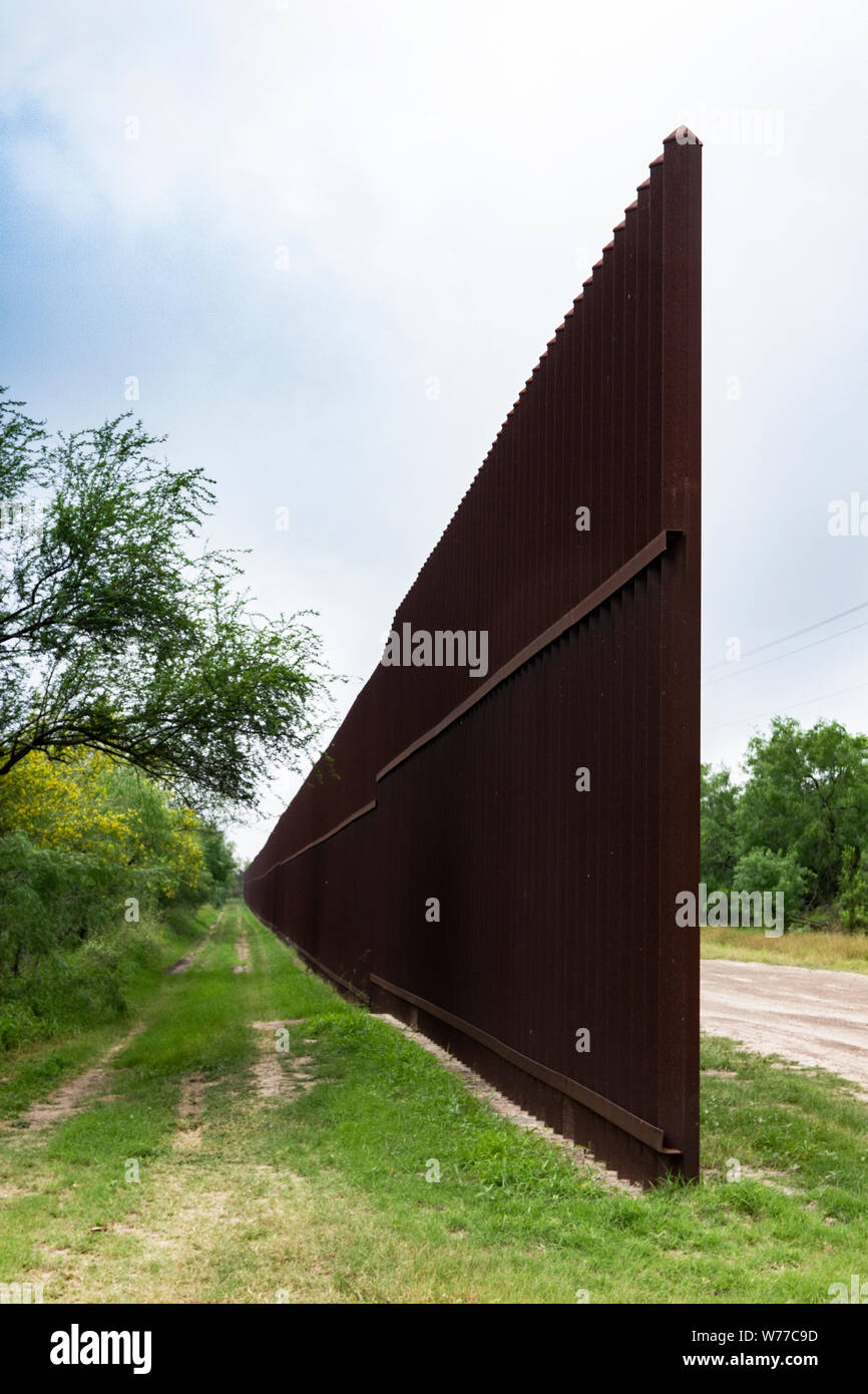 Young corn stalks grow in a field near a section of the border fence in ...