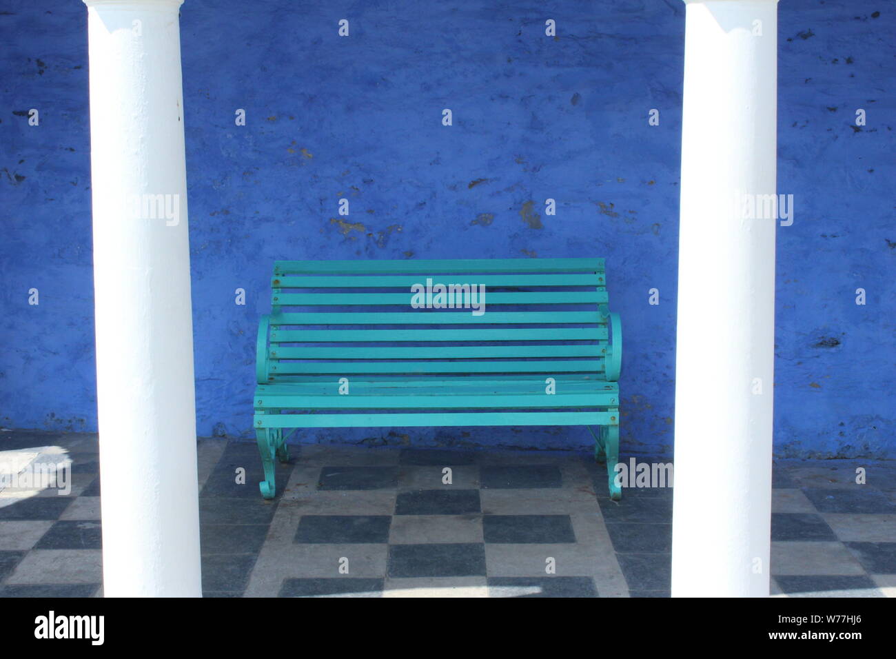 Image of a bright blue bench in front of a dark blue wall, behind two ...