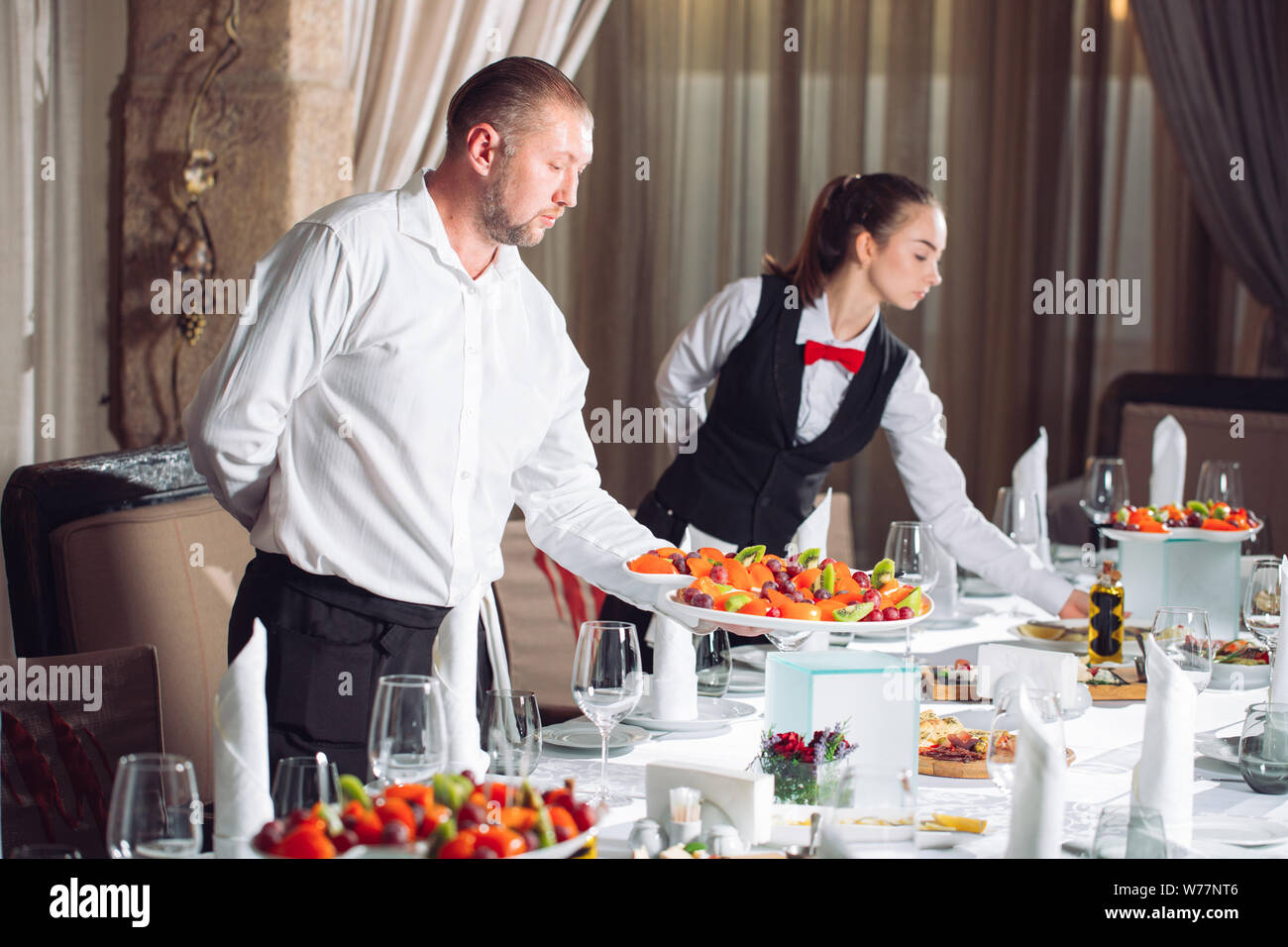 Waiters serving table in the restaurant preparing to receive guests ...