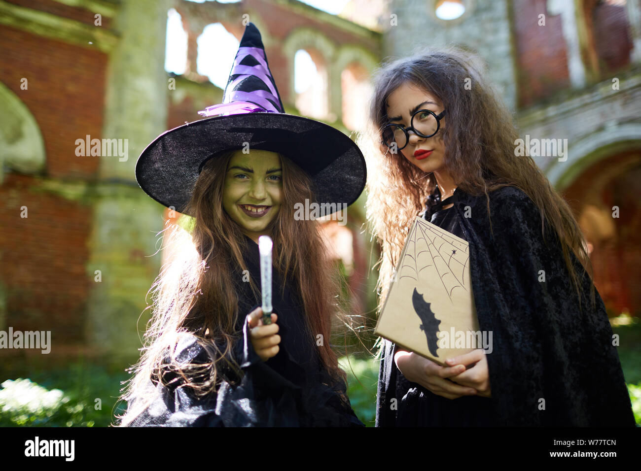 Waist up portrait of two little witches looking at camera while posing ...