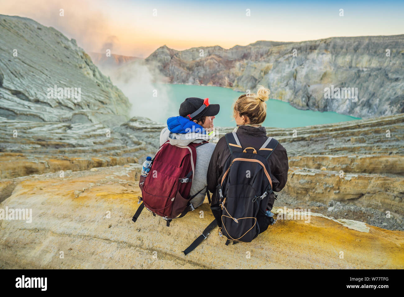 Young tourist man and woman sit at the edge of the crater of the Ijen ...