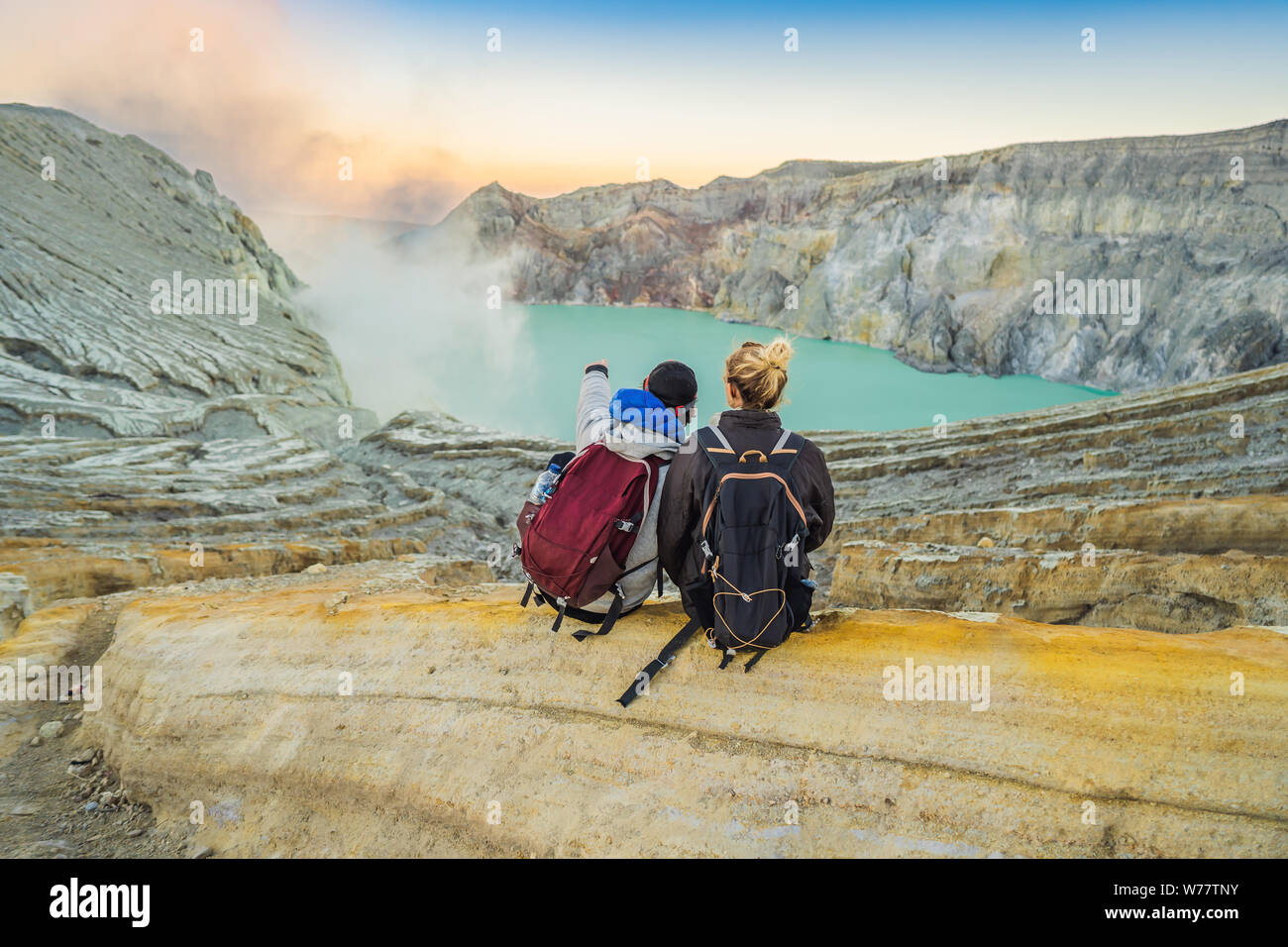 Young tourist man and woman sit at the edge of the crater of the Ijen ...