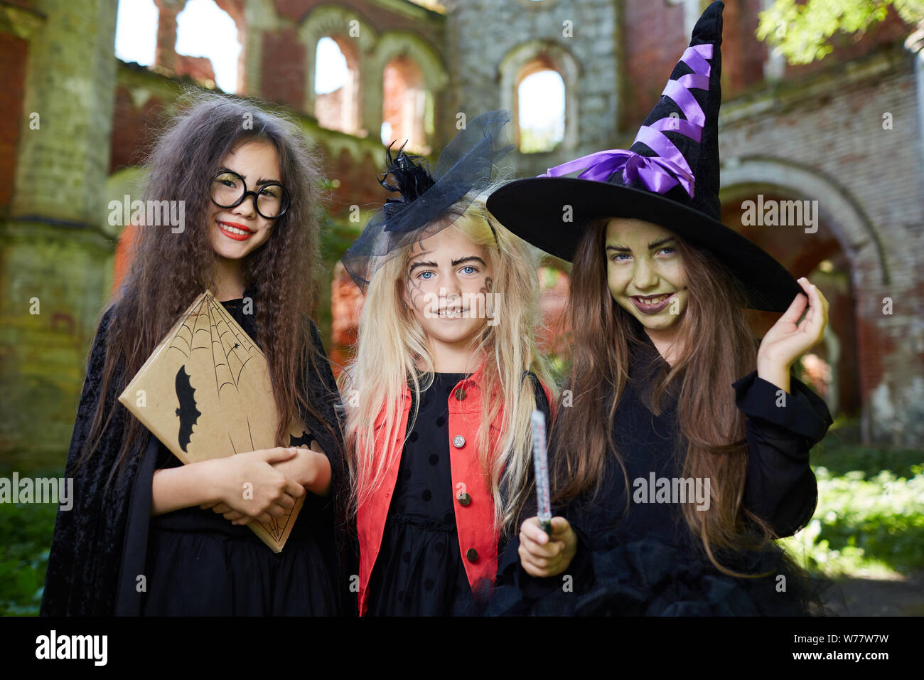 Waist up portrait of three little witches looking at camera while ...
