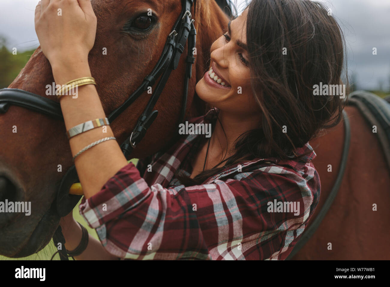 Portrait of beautiful woman and horse at the horse farm. Cowgirl petting her horse and smiling ...