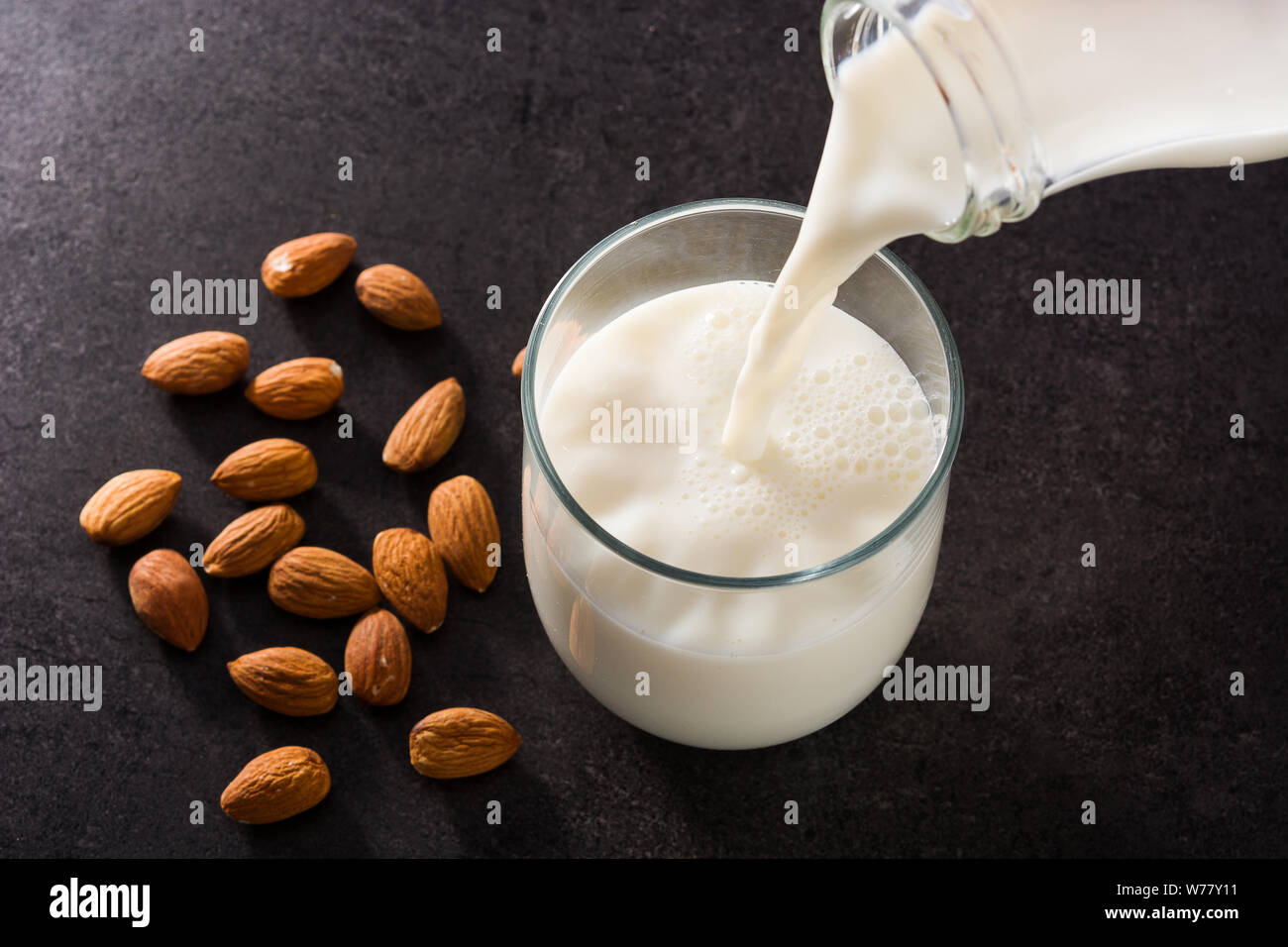 Pouring almond milk in glass on black background Stock Photo - Alamy