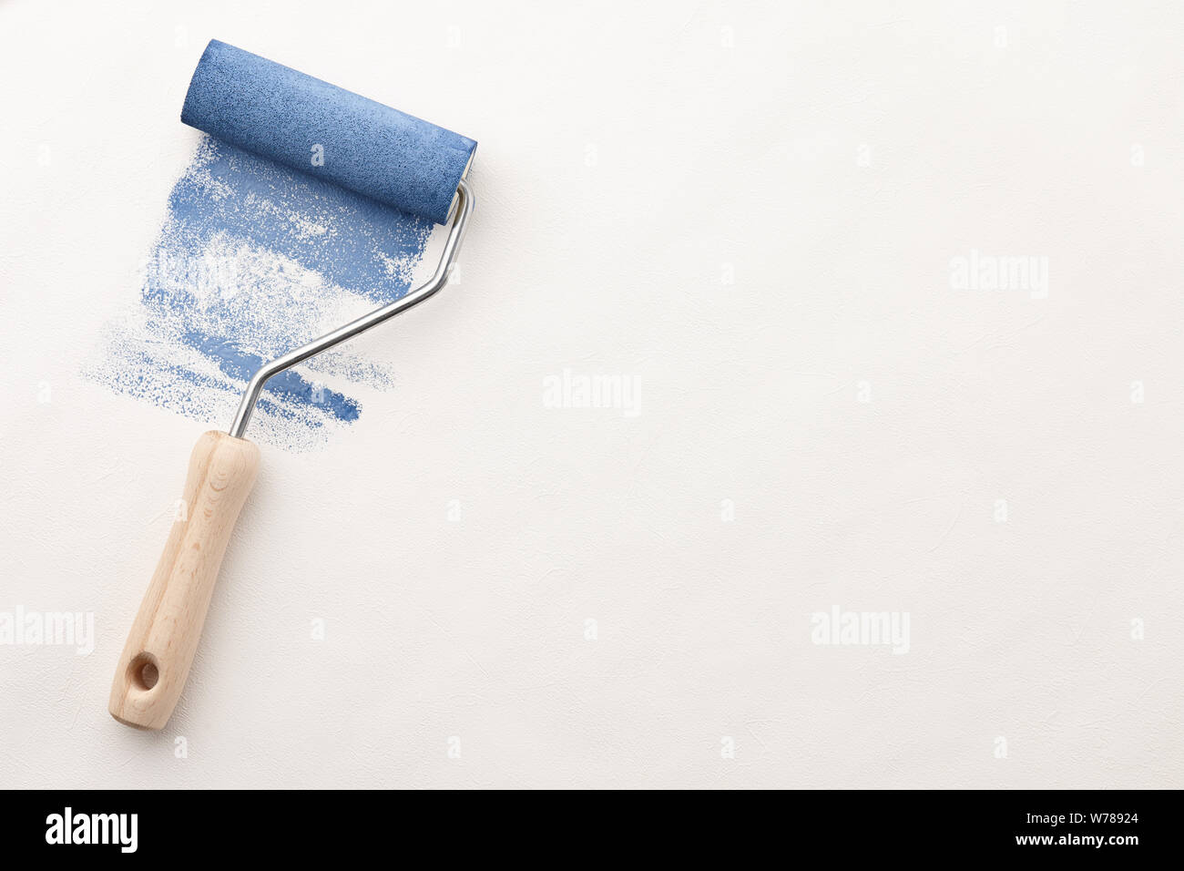 Roller with blue paint on wallpaper background Stock Photo - Alamy