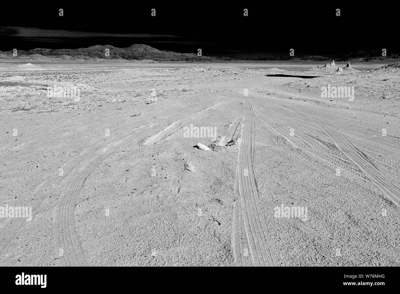 Flat empty barren desert landscape with tire tracks under black skies ...