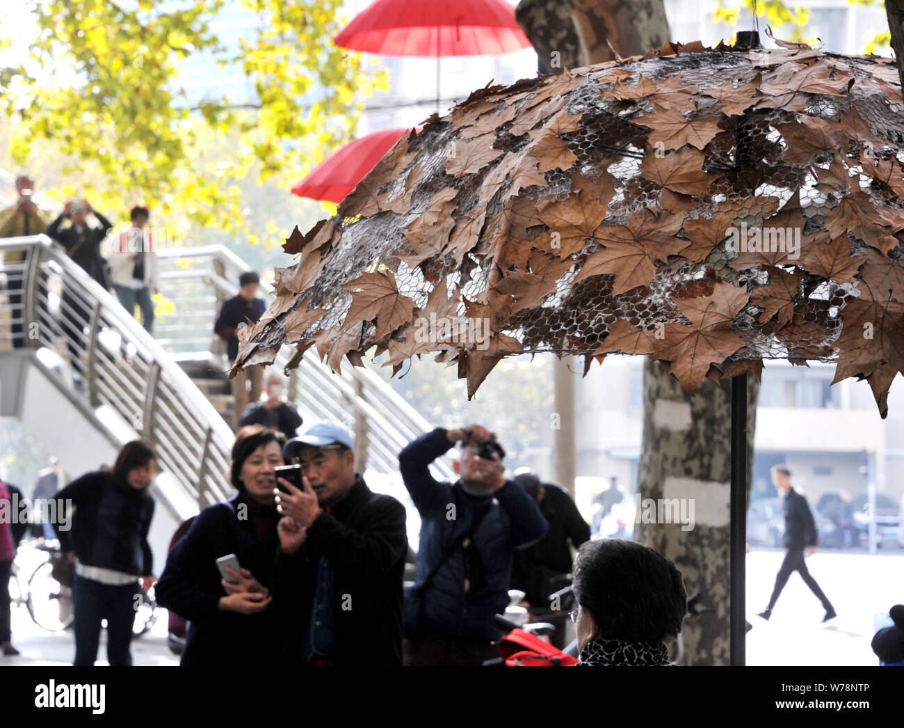 Chinese pedestrians take photos of a "leaves umbrella" installation ...