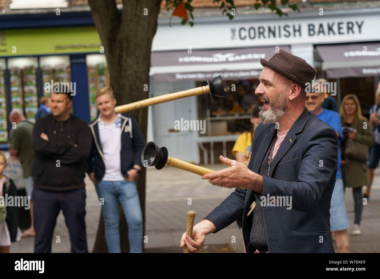 Street performer entertaining shoppers by juggling with toilet plungers ...