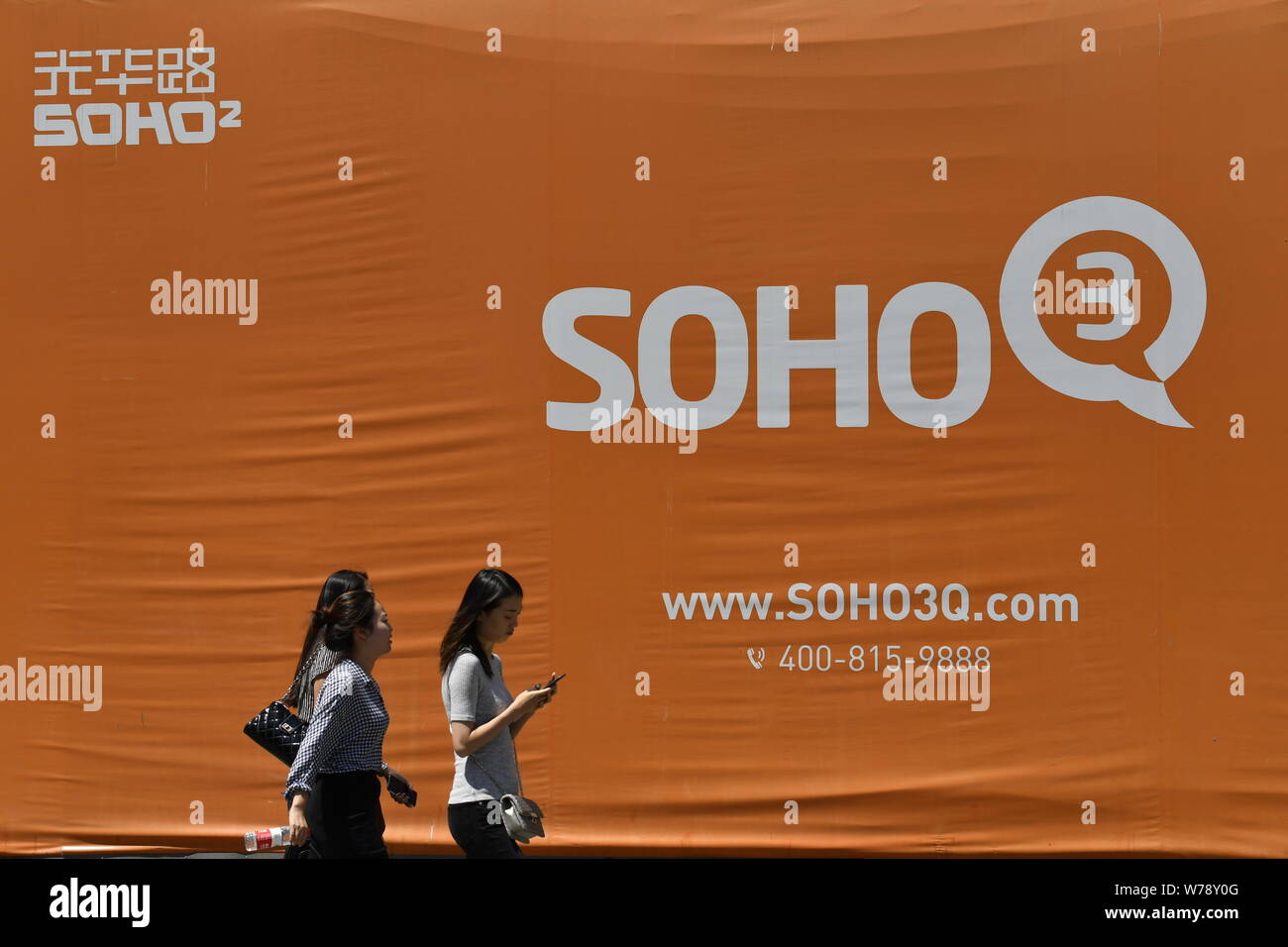 --FILE--Pedestrians walk past an advertisement of SOHO 3Q, shared office brand of SOHO China, at ...