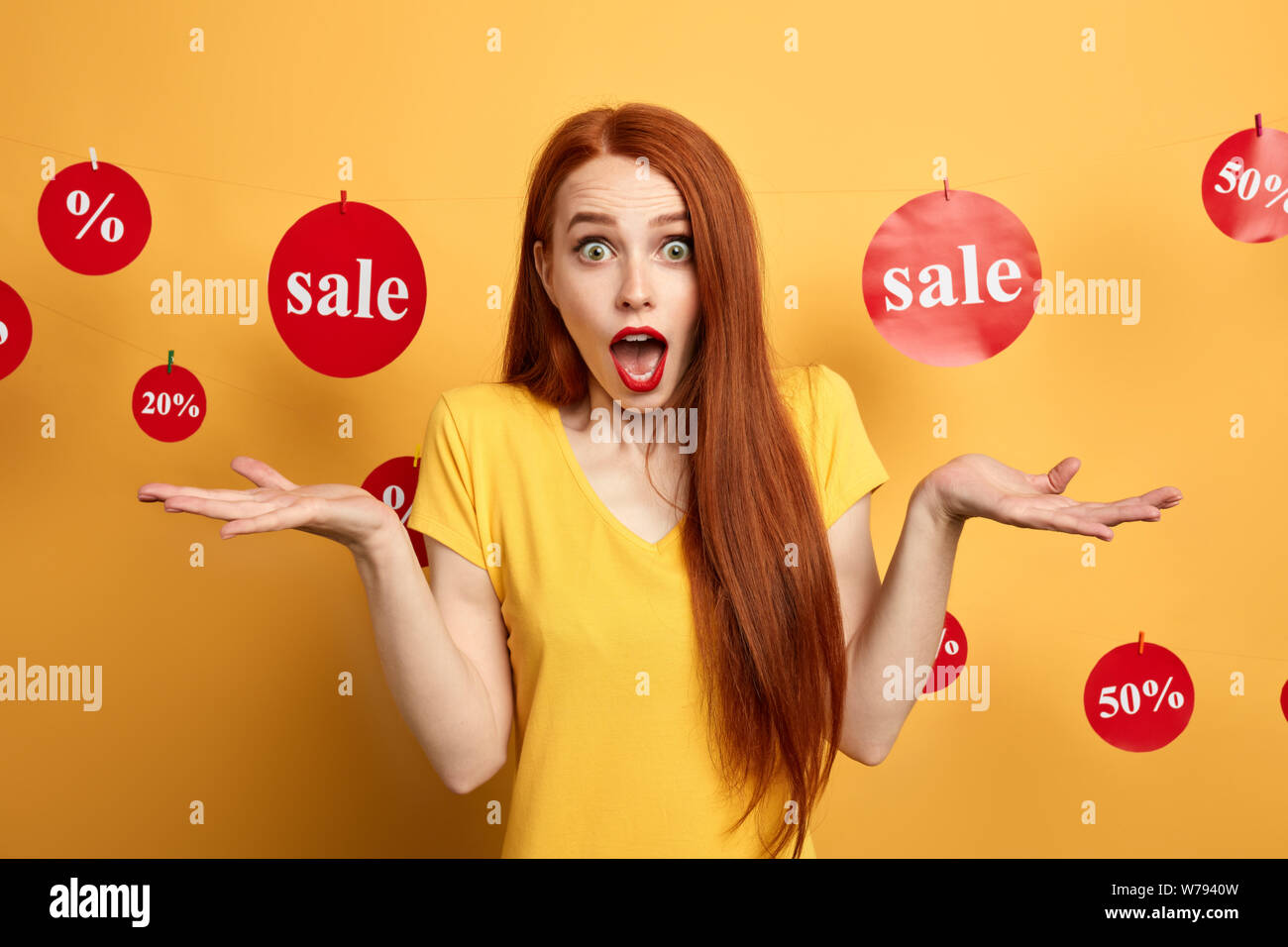 Surprised young woman with raised arms shouting,shrugging her shoulders ...