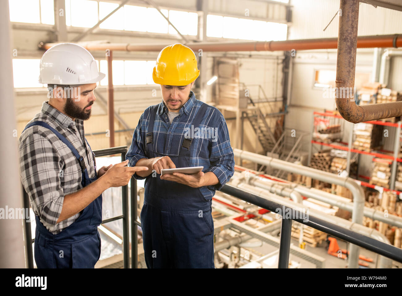 Two young engineers of large factory discussing online technical data ...