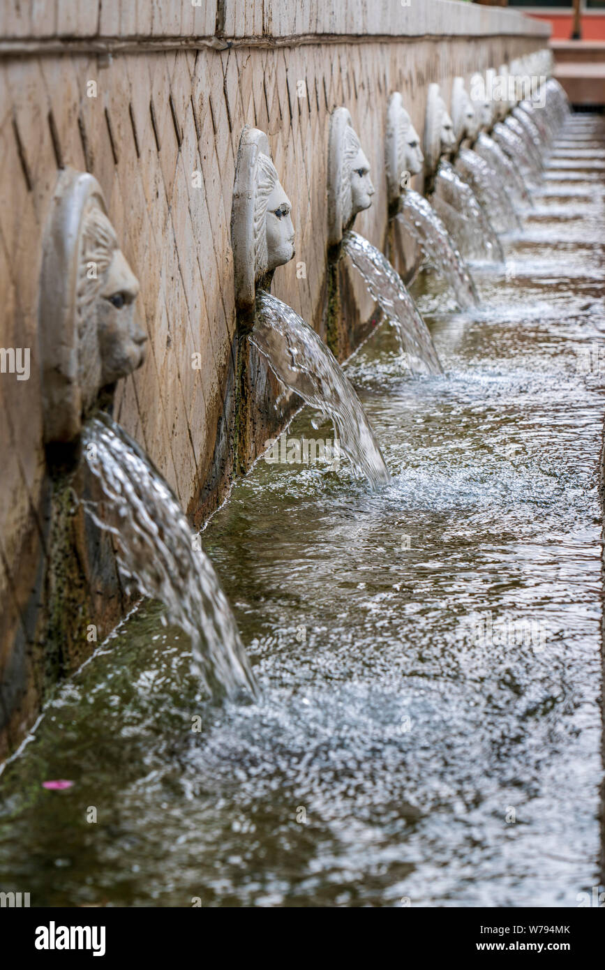 Lion heads spewing water in a long trough is a Venetian fountain in the ...