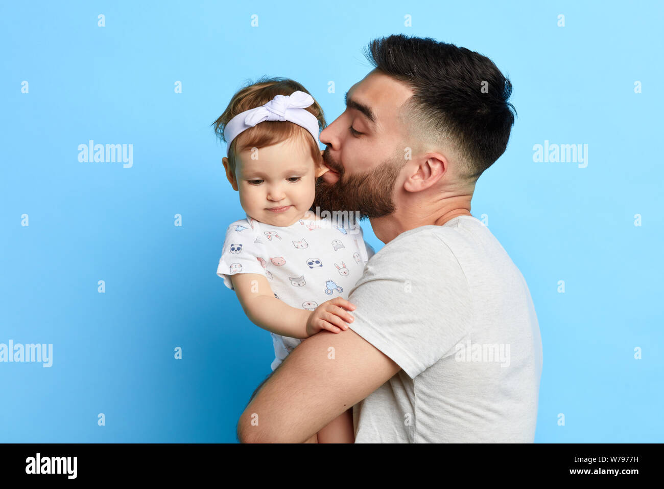 Father holding his little daughter, having fun with her, biting her ear ...