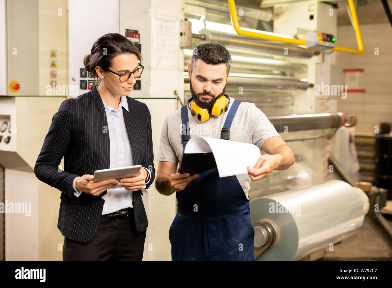 Two factory workers reading document with description of new technical ...