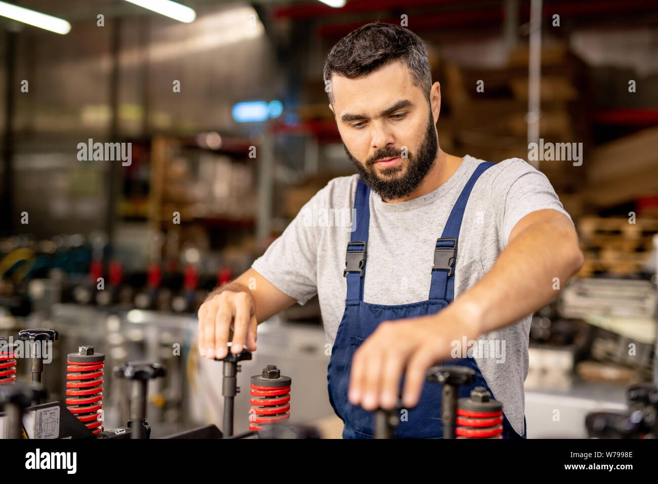 Serious young factory worker setting industrial machine in workshop ...
