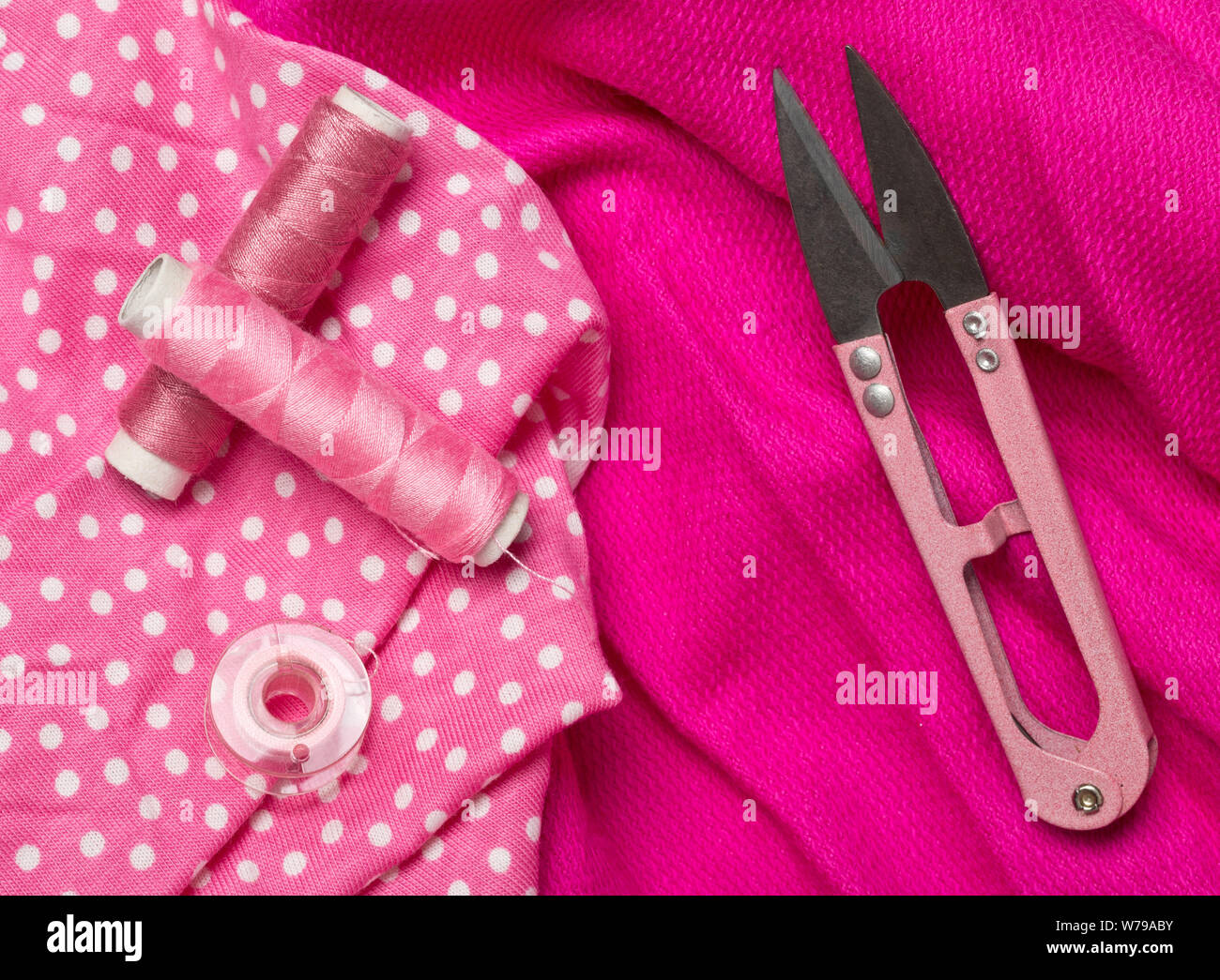 Pink colored flat lay top view sewing tools with thread and scissors on ...