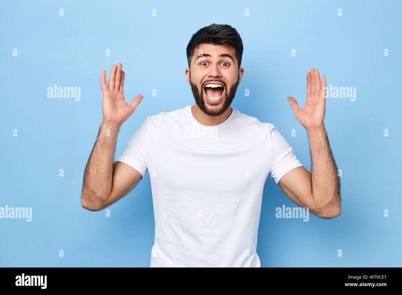 Young emotional man in casual clothes shouting with raised arms ...
