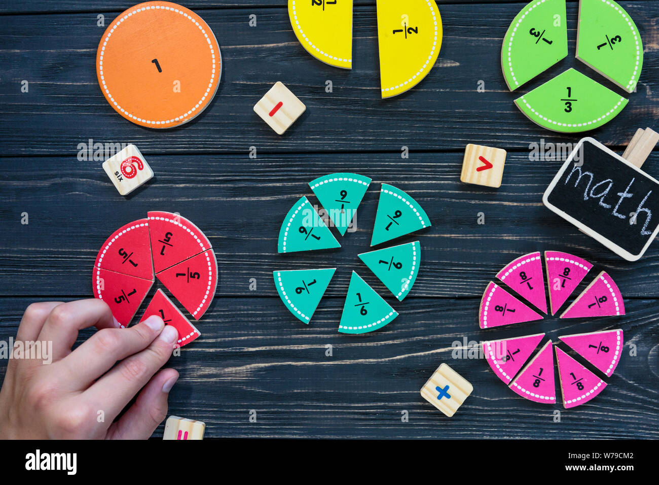Kids hand moves colorful math fractions on dark wooden background or ...