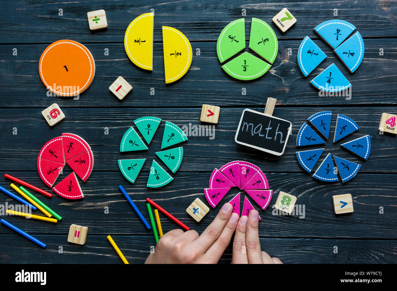 Kids hand moves colorful math fractions on dark wooden background or ...