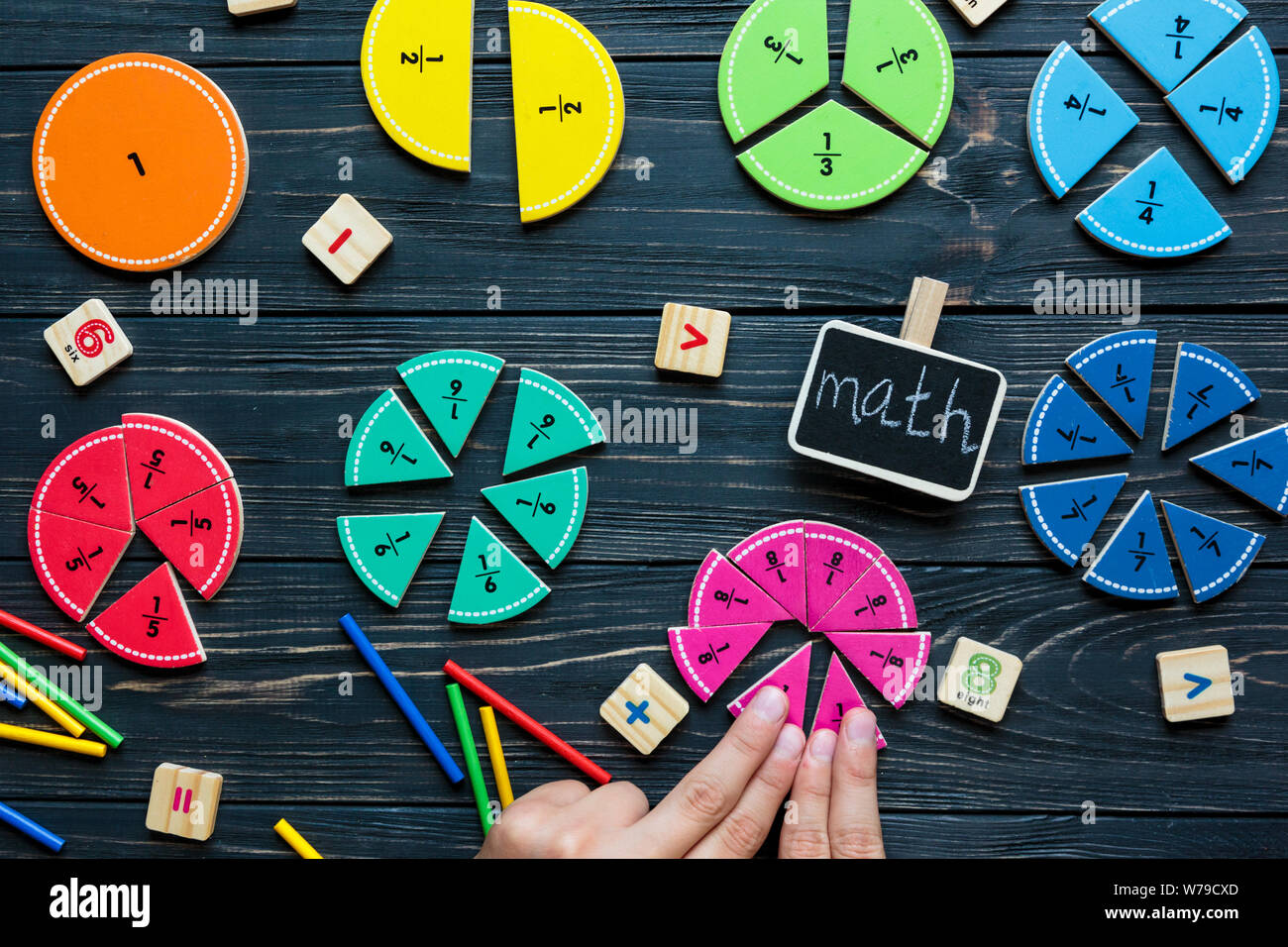 Kids hand moves colorful math fractions on dark wooden background or ...