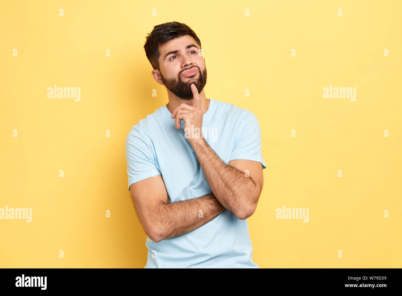 good looking man with finger on his chin looking up, isolated blue ...