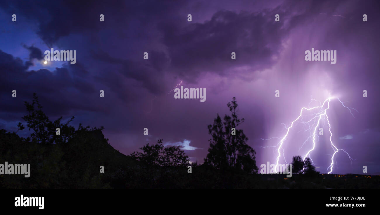 The moon is still visible as a lightning storm moves in Stock Photo - Alamy