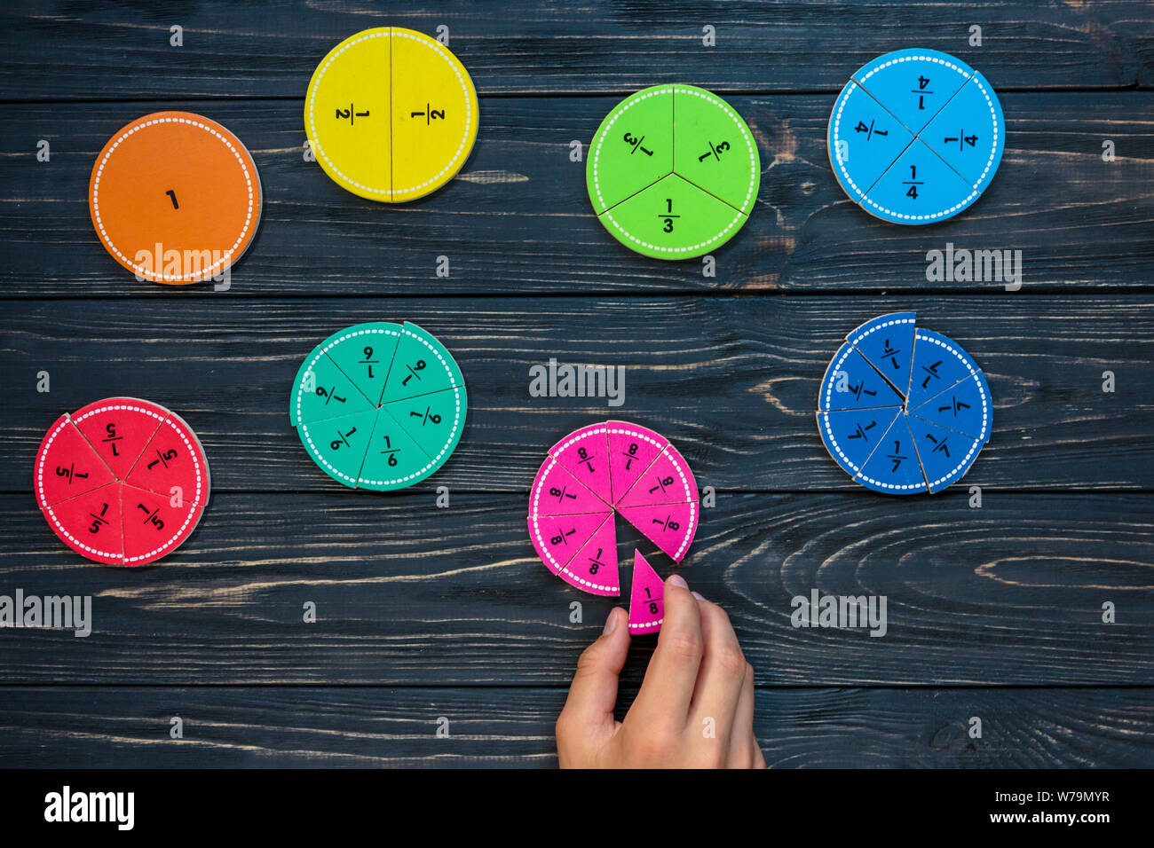 Kids hand moves colorful math fractions on dark wooden background or ...