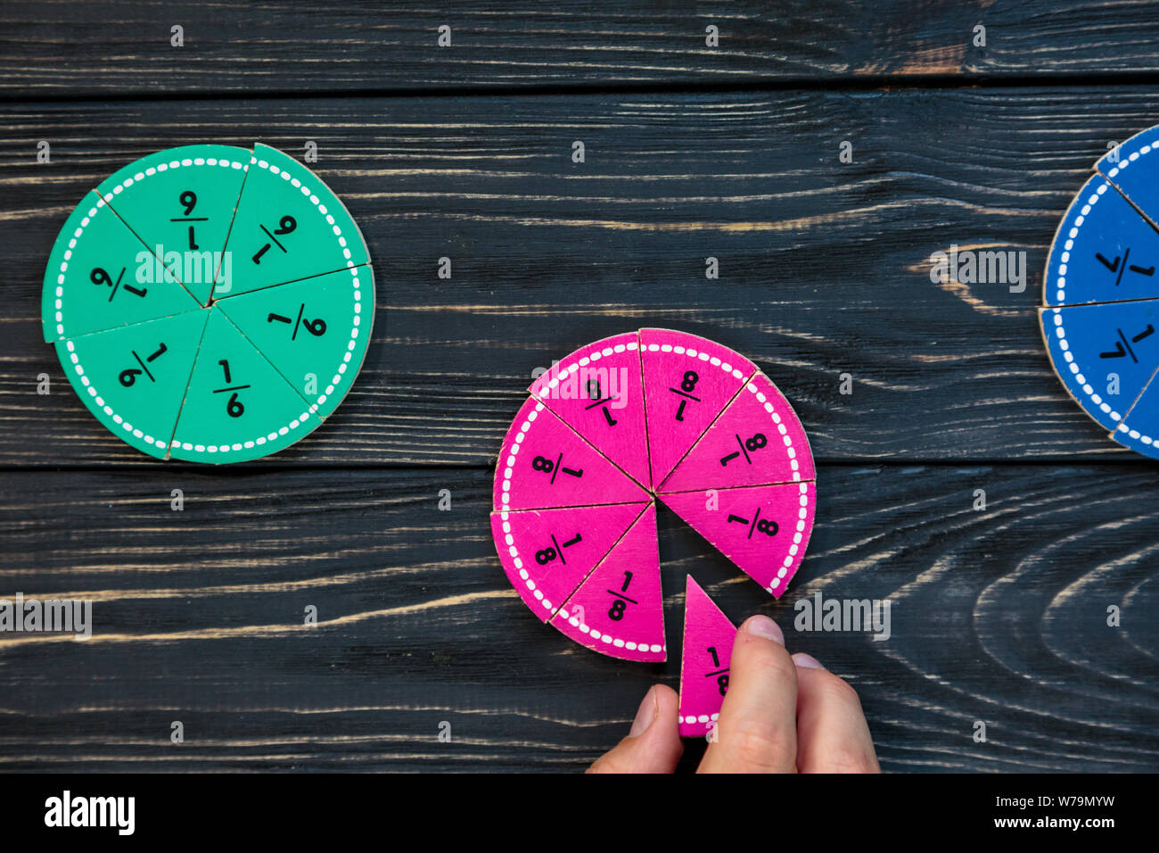 Kids hand moves colorful math fractions on dark wooden background or ...