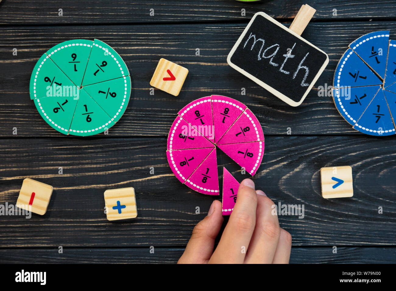 Kids hand moves colorful math fractions on dark wooden background or ...