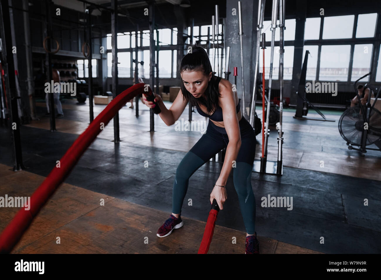 Fit woman using battle ropes during strength training at the gym ...