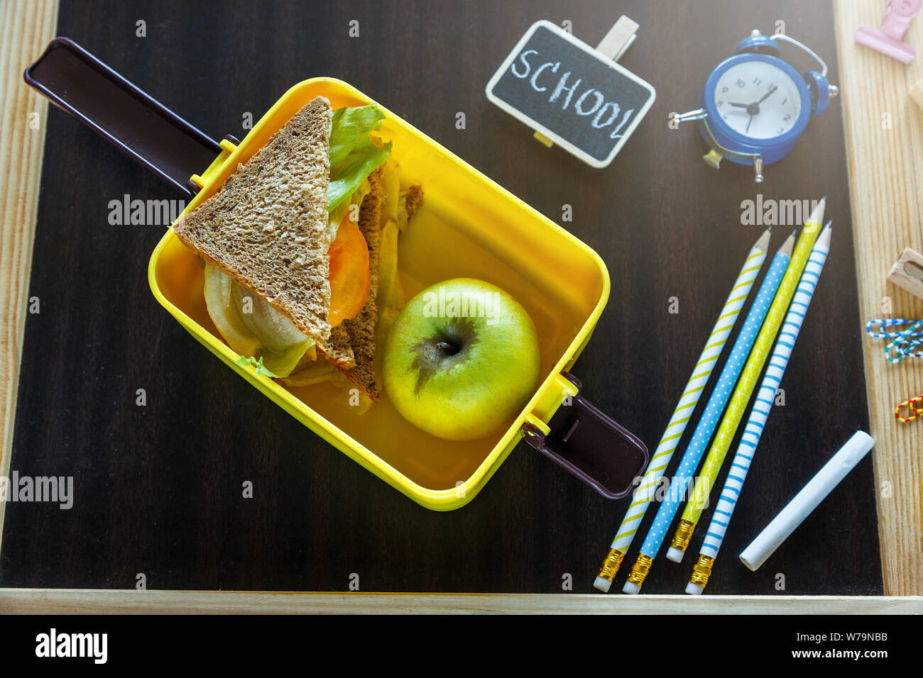 School yellow lunch box with sandwich, green apple, clock on chalkboard ...