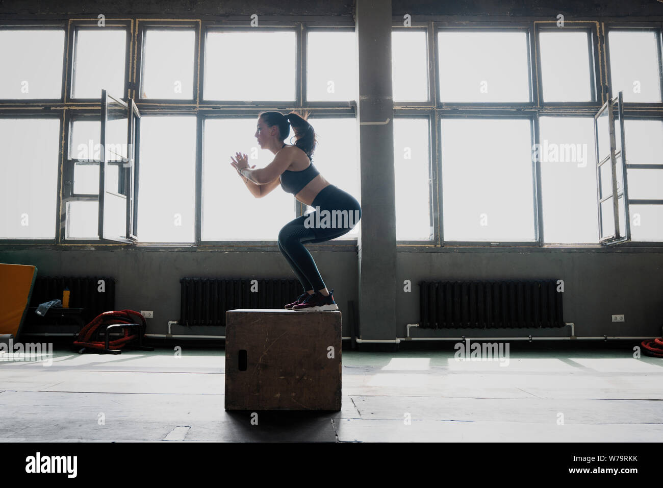 Fit young woman box jumping at a crossfit style gym. Female athlete is ...