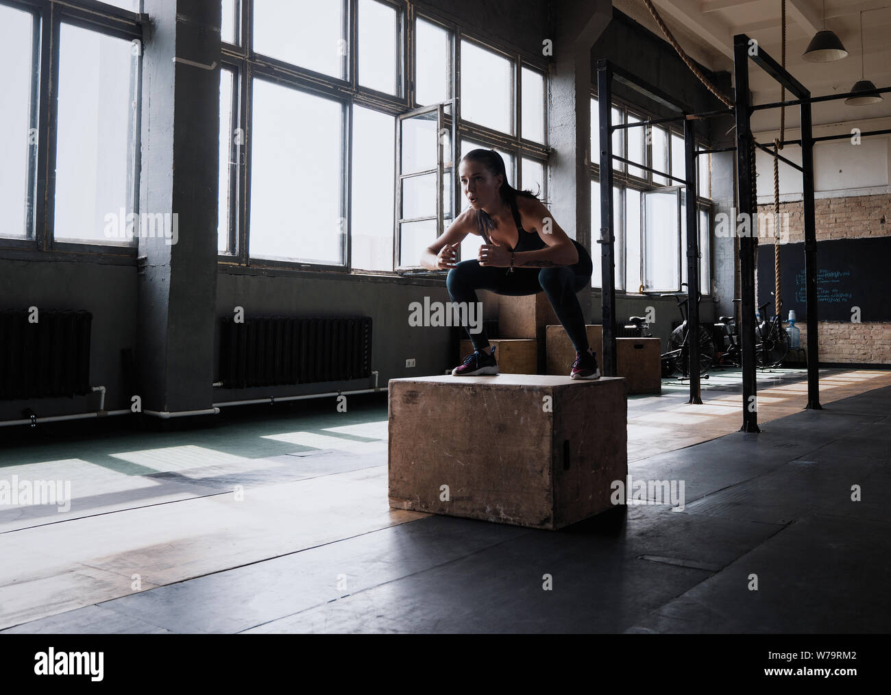 Fit young woman box jumping at a crossfit style gym. Female athlete is ...