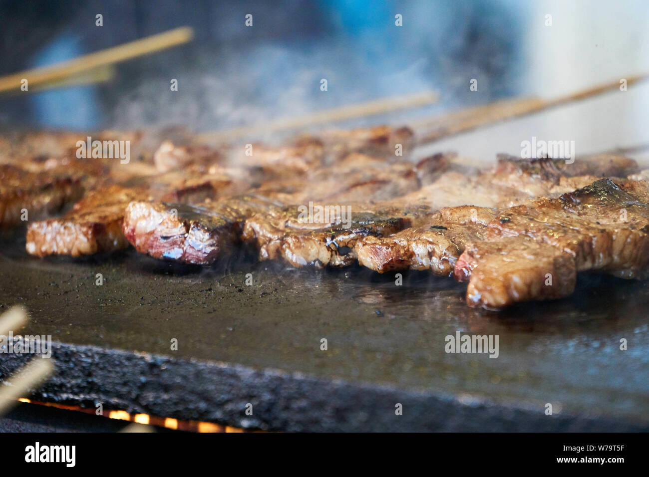 Beef slices on skewers cook on a teppanyaki grill at a street food ...