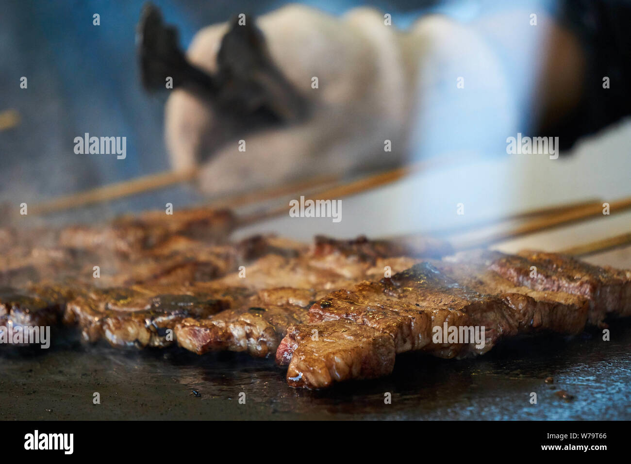 Beef slices on skewers cook on a teppanyaki grill at a street food ...