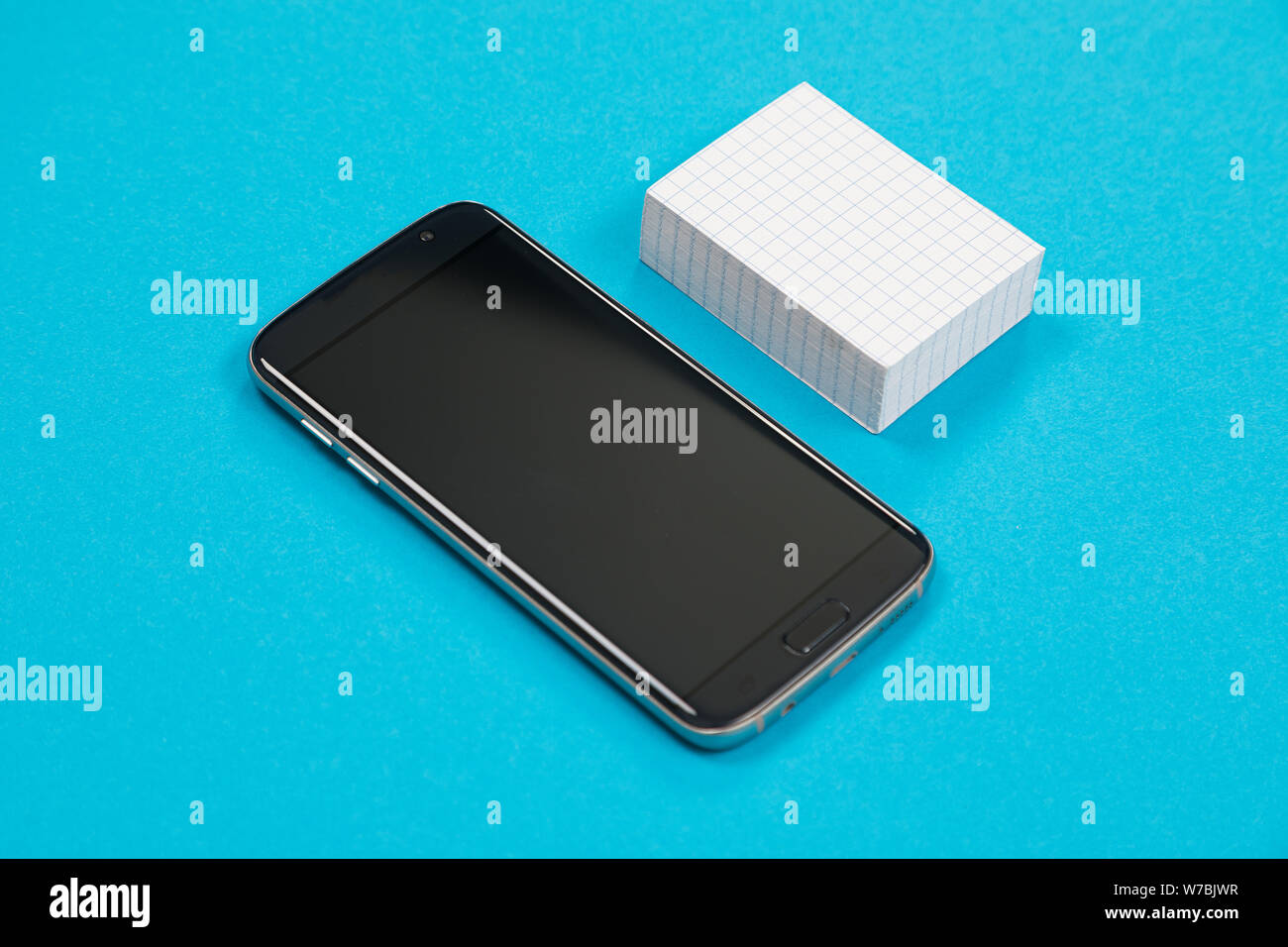 Black mobile phone and a pile of white scratch paper are lying on azure ...