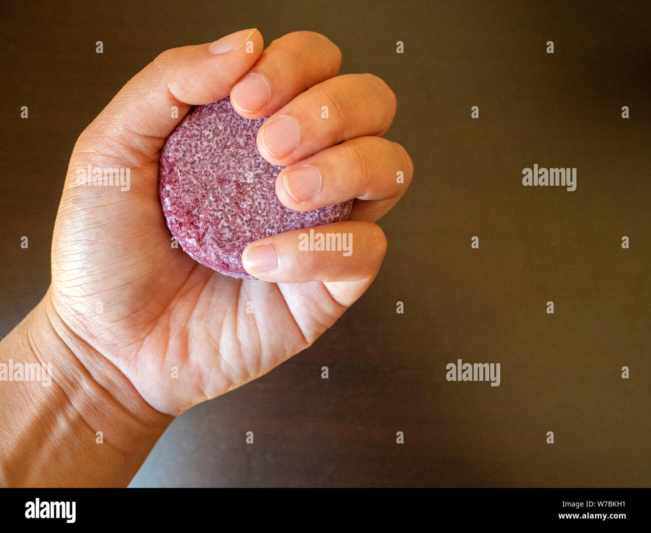 Hand grasping a red Shampoo bar before washing their hair in the shower ...
