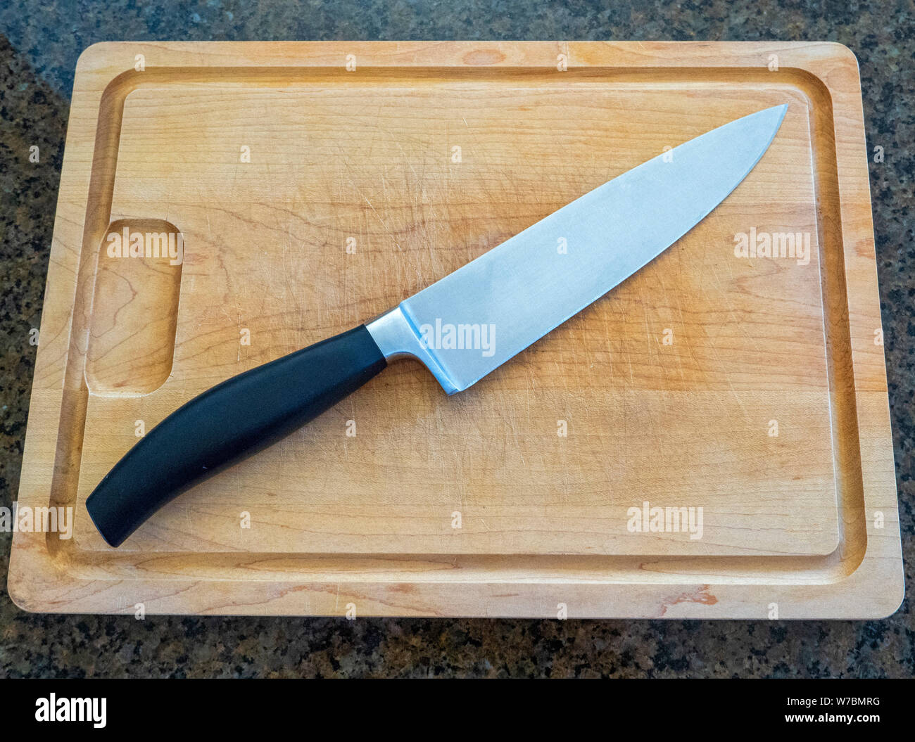 Isolated large chef’s knife on a large wooden cutting board with a ...