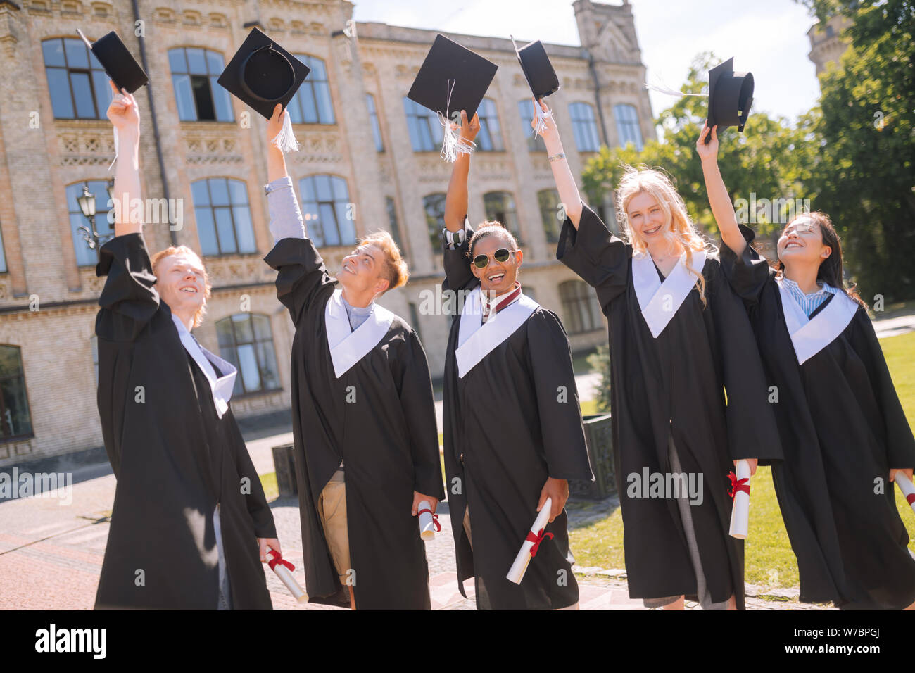Cheerful graduates raising their masters caps in the air Stock Photo ...