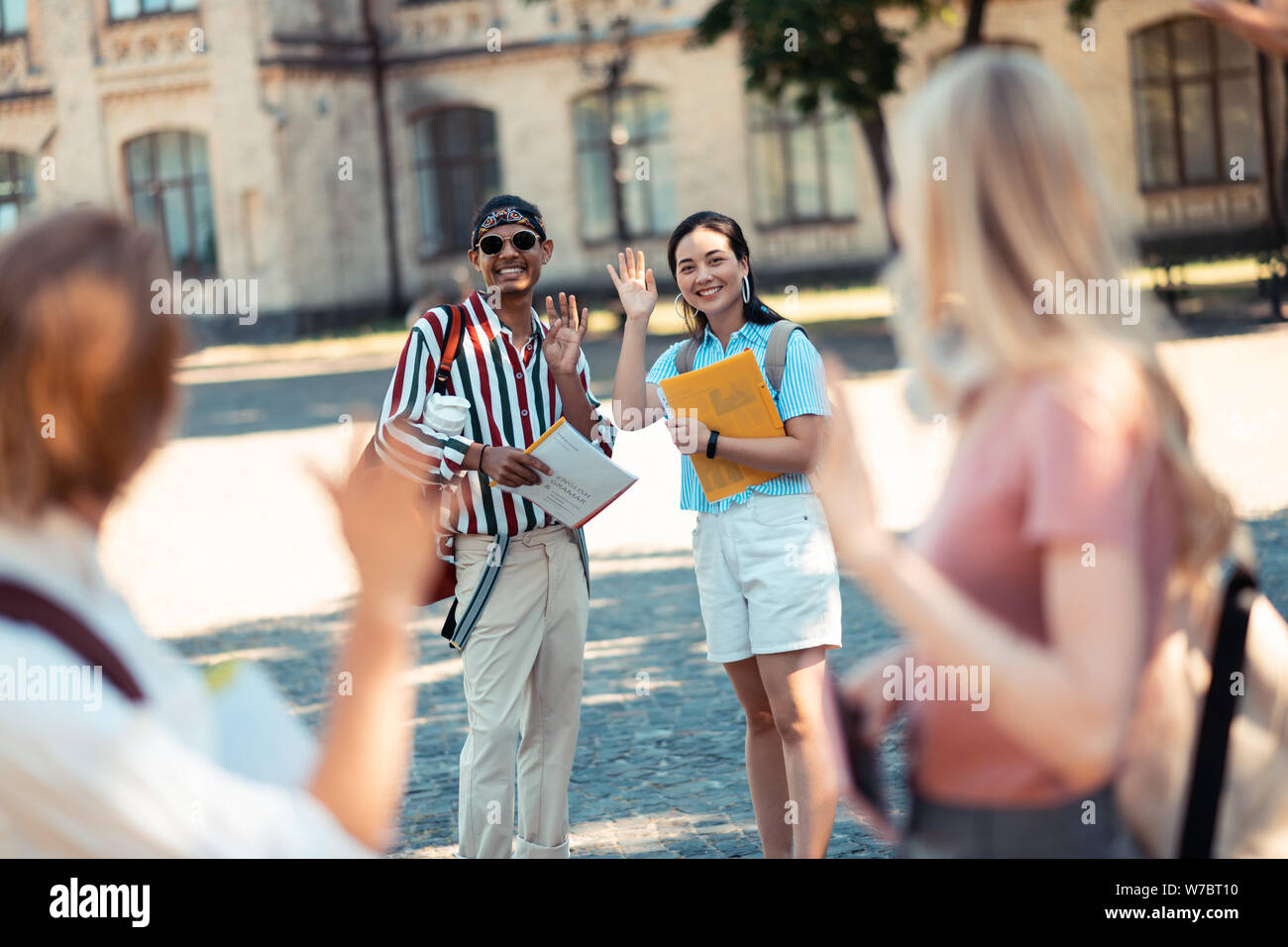 Two students waving hands to their groupmates in the front Stock Photo ...