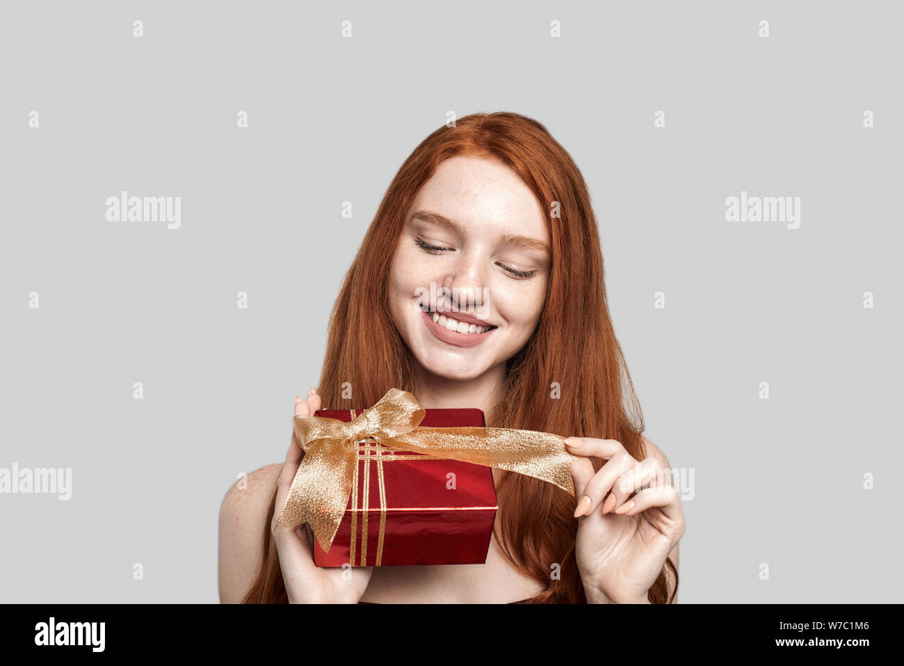 Studio shot of cute and young redhead woman opening a gift box and ...